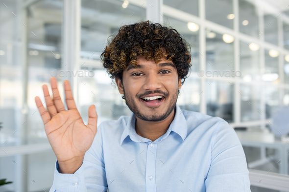 Cheerful young man waving hello in modern office setting Stock Photo by ...