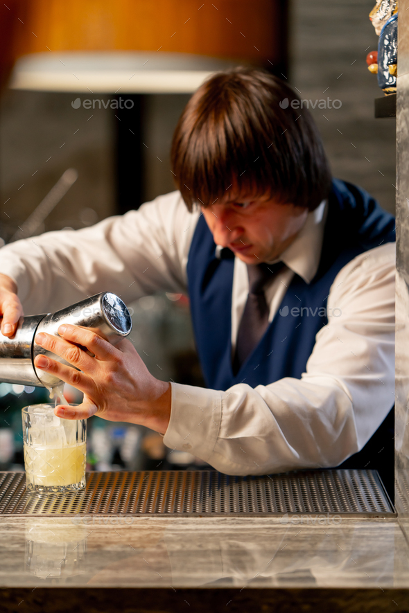 in a Japanese restaurant behind the bar bartender pours a cocktail from ...