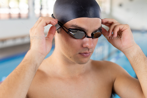 Caucasian young male swimmer adjusting goggles indoors, standing by ...