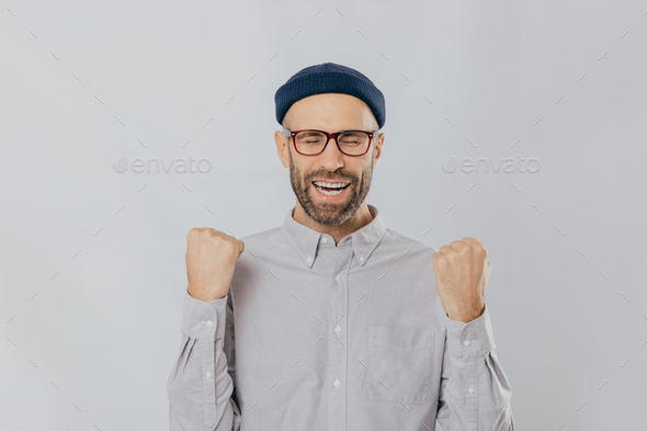 Joyful man with glasses clenching fists in excitement, celebrating a ...