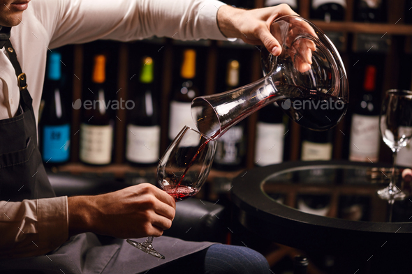 Sommelier pouring red wine from bottle into decanter at table in ...