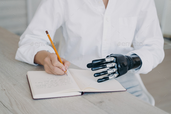Thoughtful woman with a bionic arm pens ideas in a notebook Stock Photo ...