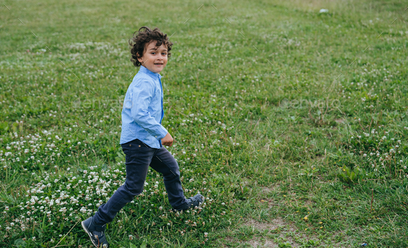 Playful young boy with curly hair running joyfully across blooming ...