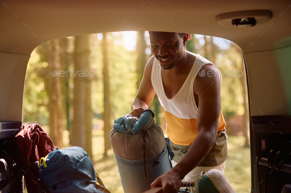 Happy black man packing camping equipment into his van. Stock Photo by ...