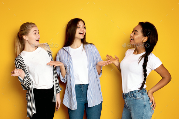 Three Girls Engaging in Lively Conversation Against Vibrant Yellow ...
