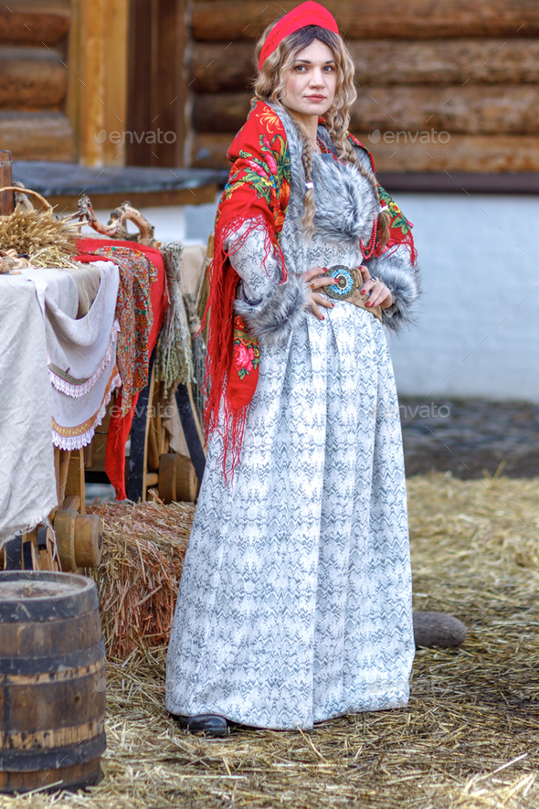 A girl in traditional Russian clothes and a kokoshnik stands at a table ...