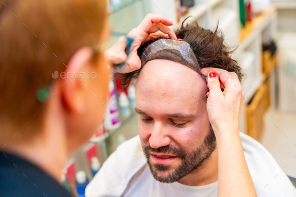 Hairdresser attaching a capillary prosthesis carefully to a man's head ...
