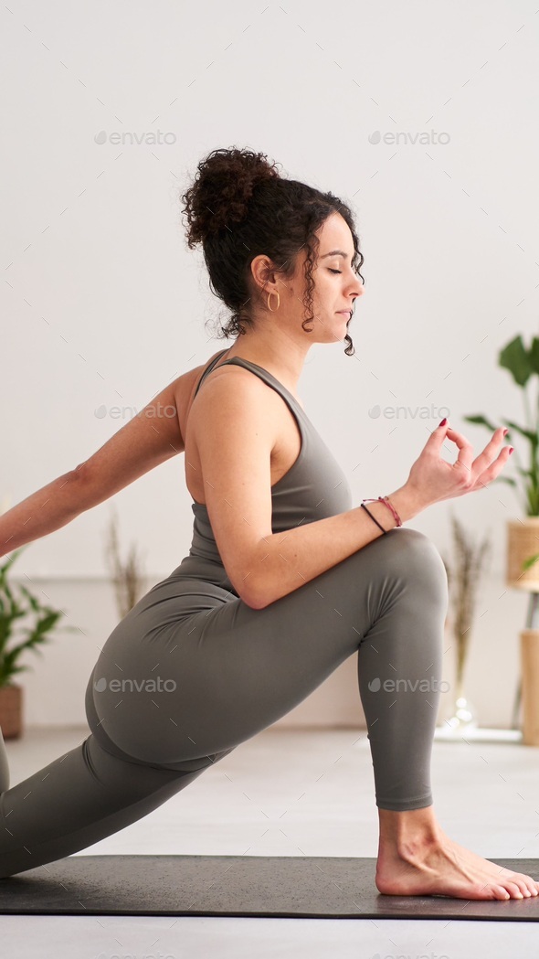 Side view of young caucasian girl in grey sportswear doing yoga. One ...