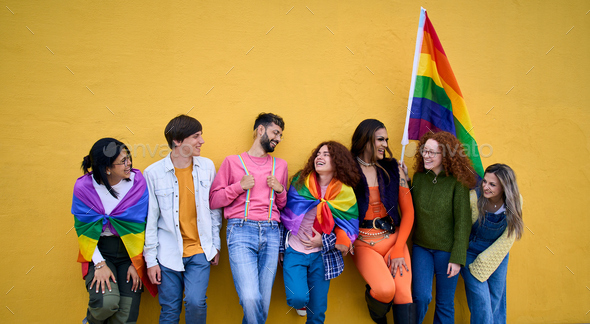 Group of diverse LGBT young people standing on wall yellow. Smiling ...
