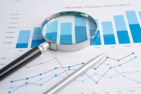 Magnifying glass on spreadsheet and graph paper. Stock Photo by chormail