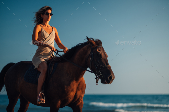 Low angle portrait of a female rider riding her horse at the seacoast ...