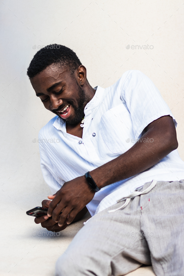 Black man laughing while browsing on mobile phone Stock Photo by ...