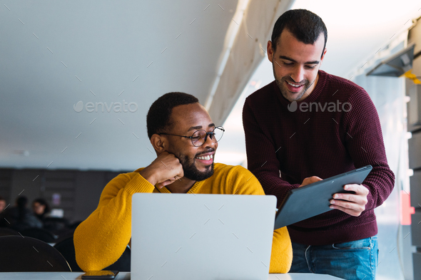 Positive diverse guys with laptop and tablet in modern workspace Stock ...