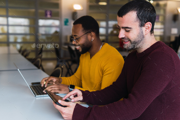 Positive diverse guys with laptop and tablet in modern workspace Stock ...