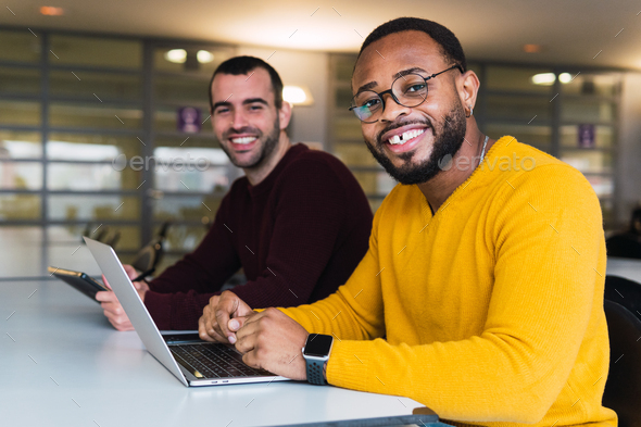 Positive diverse guys with laptop and tablet in modern workspace Stock ...