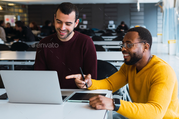 Positive diverse guys with laptop and tablet in modern workspace Stock ...