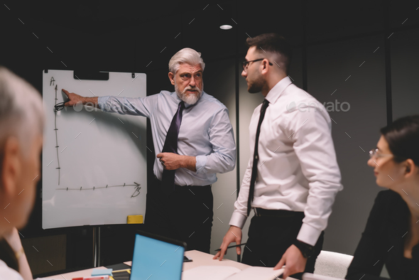 Aged boss pointing at flip chart explaining strategy to employee Stock ...