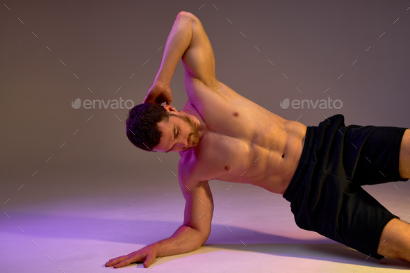 muscular bodybuilder leaning on arm and right hand while doing exercise ...