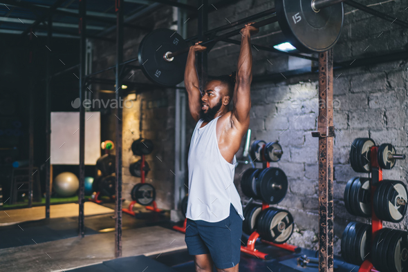 Strong black man pushing barbell over head Stock Photo by GaudiLab
