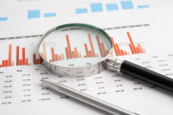 Magnifying glass on spreadsheet and graph paper. Stock Photo by chormail