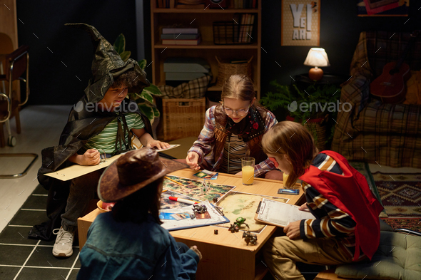 Kids bending over table with board game Stock Photo by Pressmaster