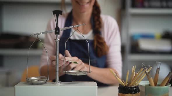 Happy woman pouring paint colors powder on vintage balance in pottery ...