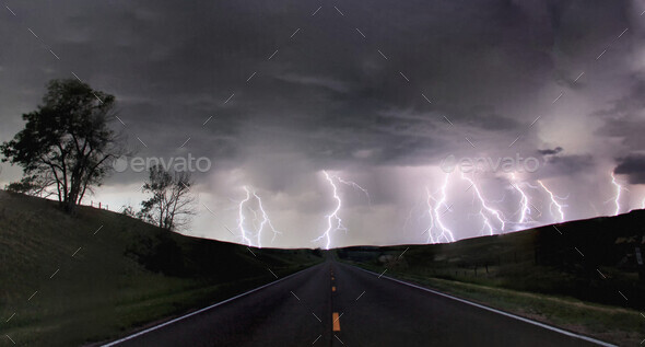 Road illuminated by multiple lightning strikes under a dark stormy sky ...