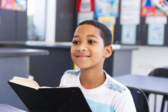Biracial boy enjoys reading a book in a classroom at school Stock Photo ...