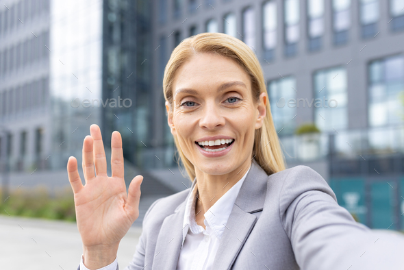 Businesswoman waving hand and smiling outside modern office building ...