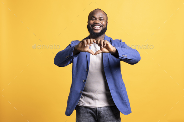Portrait of man doing heart symbol shape with hands, studio background ...