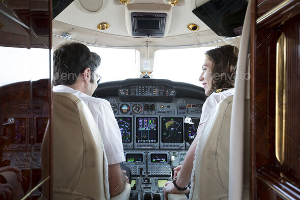 Rear view of male and female pilots talking in cockpit of private jet ...