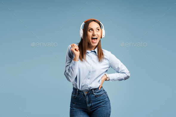 Positive young woman shouting joyfully wearing headphones, listening ...