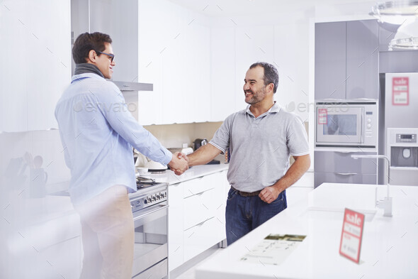 Salesman and young man shaking hands in kitchen showroom Stock Photo by ...