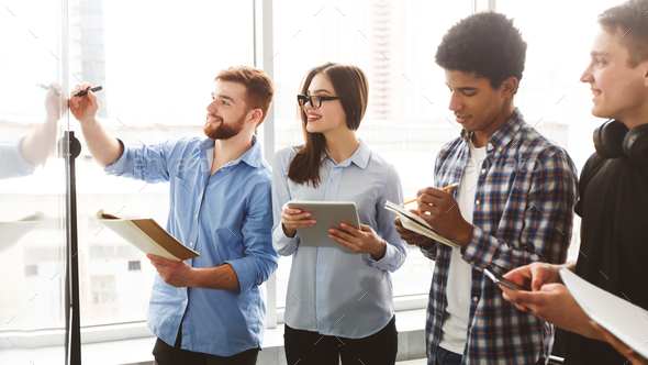 Male student writing on whiteboard in classroom, classmates taking ...