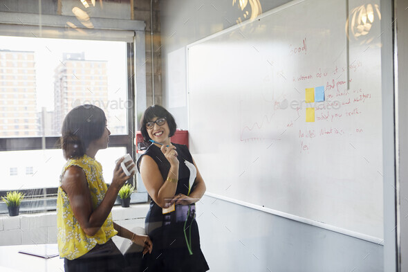 Two women in office, solving problem, using whiteboard, sticky notes ...