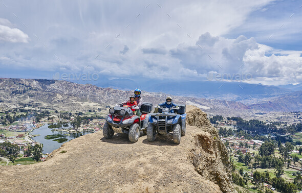 Two adventurers on ATVs posing atop a mountain with a panoramic view ...