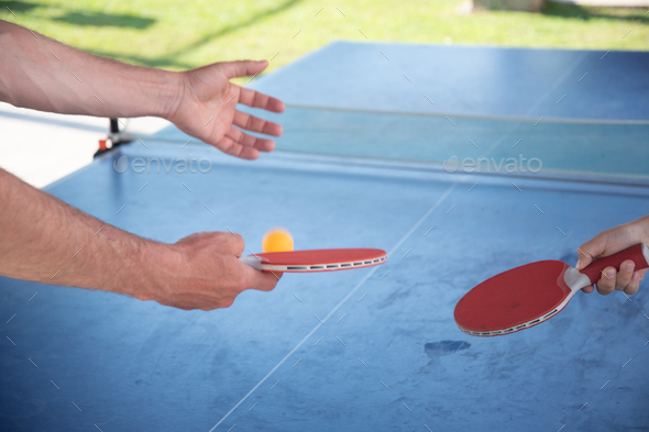 male and child's hands hold red ping pong rackets with yellow ball on a ...