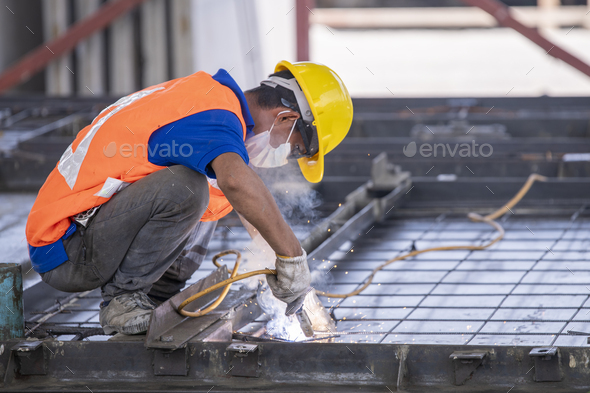 Construction worker engaged in welding work. He is crouching down on a ...