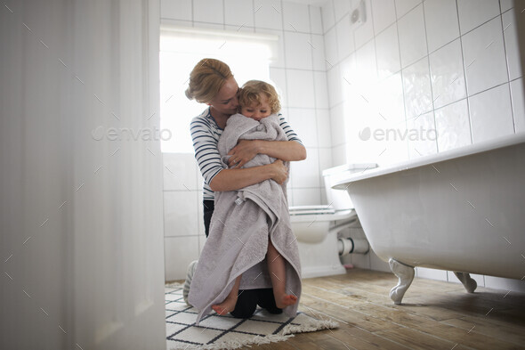 Mother and daughter in bathroom, mother wrapping daughter in bath towel ...