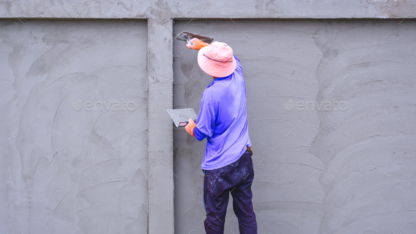 Construction worker is plastering cement on concrete fence wall, rear ...