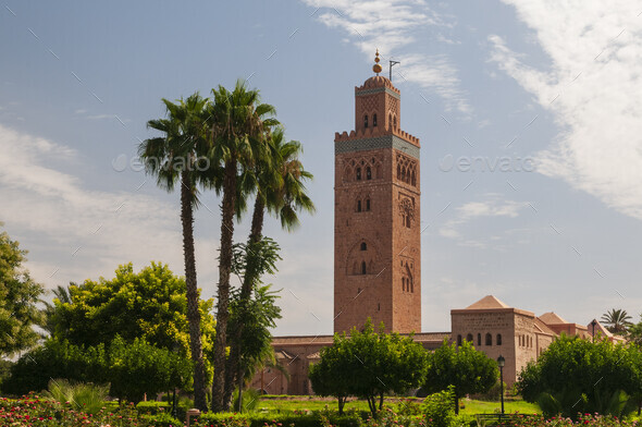 An iconic Moroccan minaret towers over lush gardens under a clear blue ...