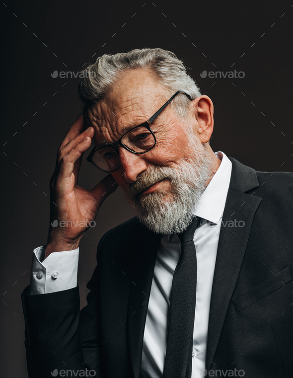Pensive old actor in formal black suit, keeps palms near his chin ...