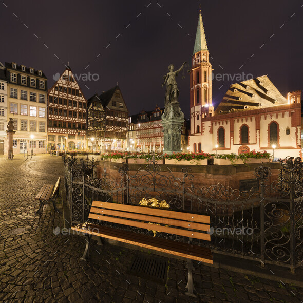 Historic European square illuminated at night with a statue and bench ...
