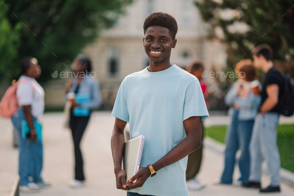 Portrait of diverse happy male student at college campus with laptop ...