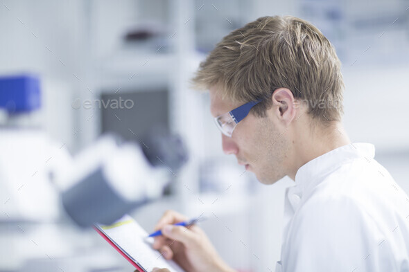 Focused young scientist recording observations in laboratory notebook ...