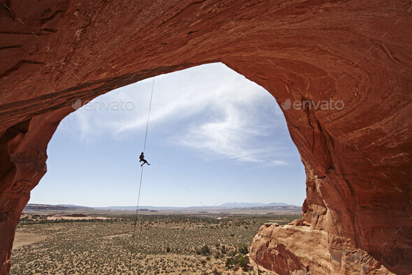 Adventurer rappelling down a majestic red rock arch Stock Photo by ...