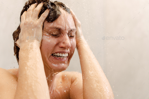 Brunette woman crying in the shower under cold water jet Stock Photo by msvyatkovska