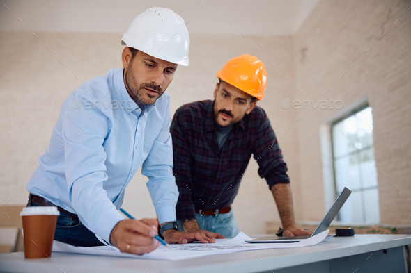 Housing project manager examining blueprints with construction worker ...