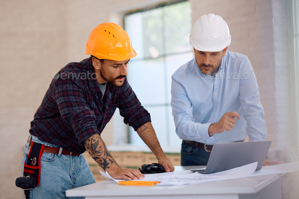 Manual worker and architect analyzing housing plans at construction ...