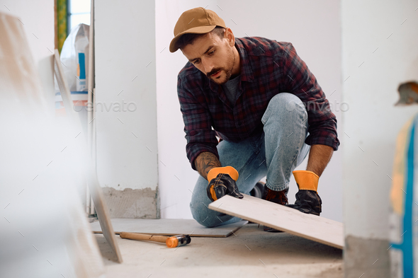 Manual worker installing floor tiles during home remodeling process ...